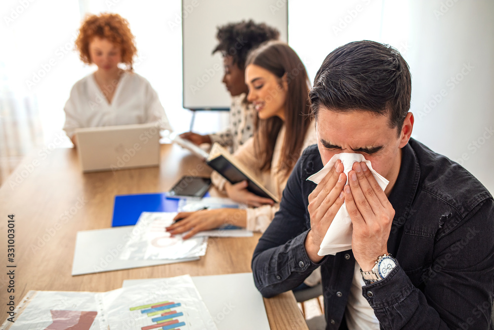Man blowing his nose while working. Young sick businessman blowing his ...