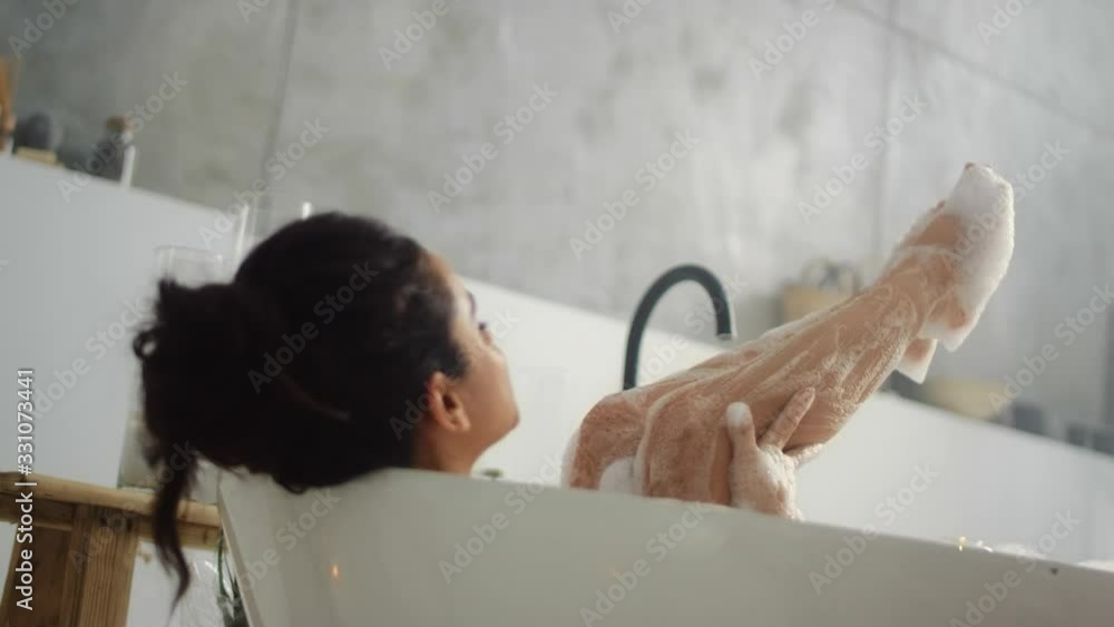 Romantic woman washing legs in foam bath. Brunette girl cleaning legs ...