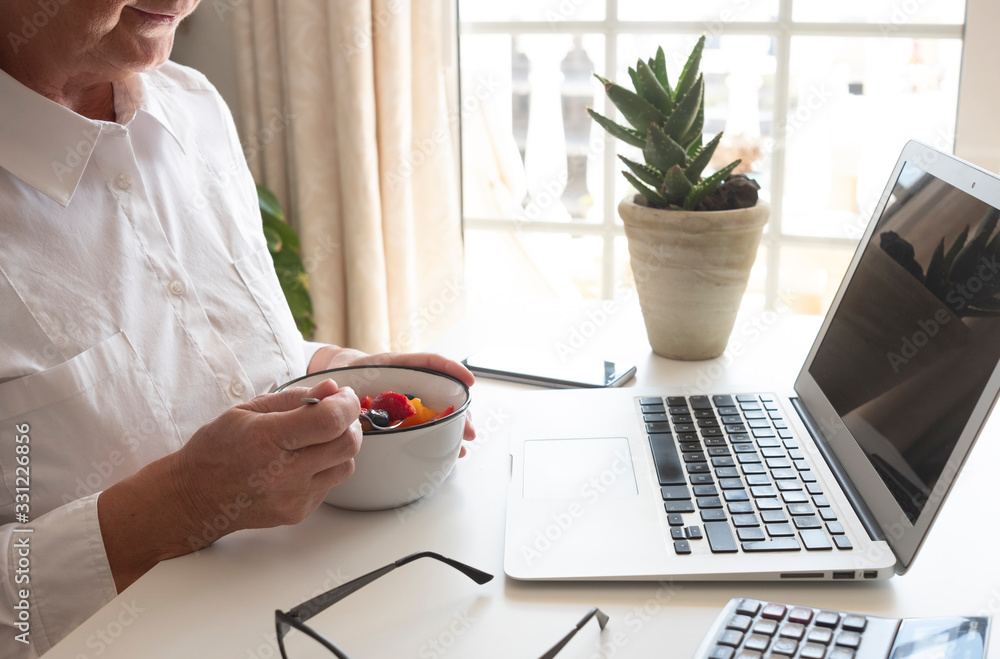 Close up view of a senior woman pausing at a desk eating a fruit salad ...