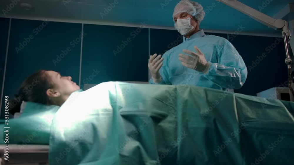 A professional mature surgeon in a robe and mask advises and soothes ...