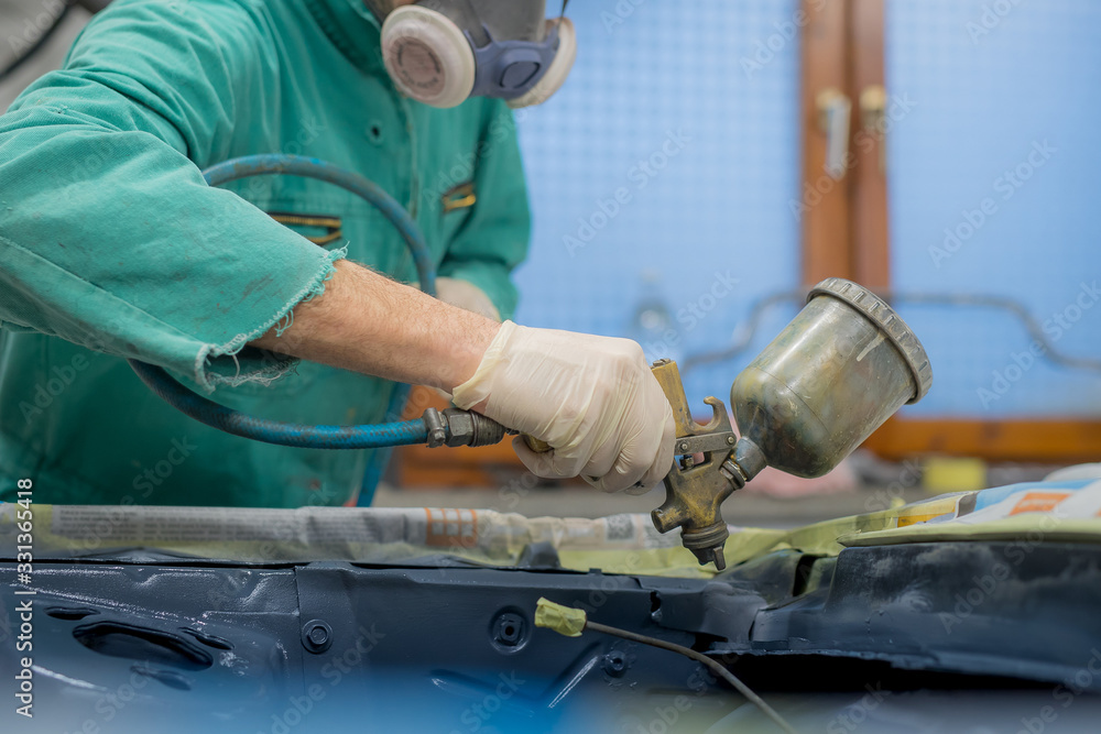 Man in green overalls preparing an engine bay of a car for a final coat ...
