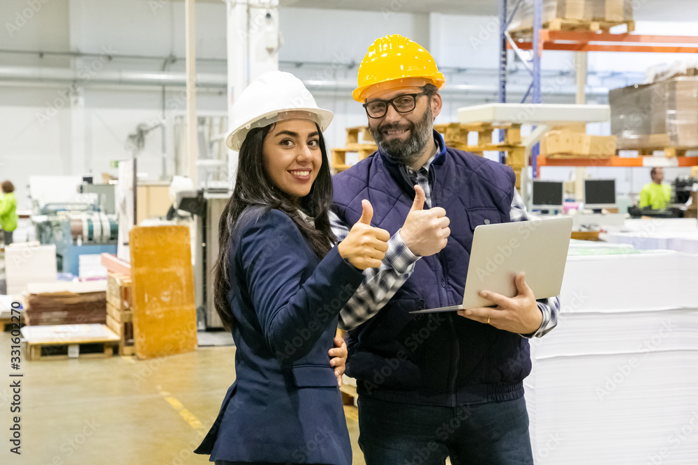 Smiling factory workers showing thumbs up. Front view of cheerful ...
