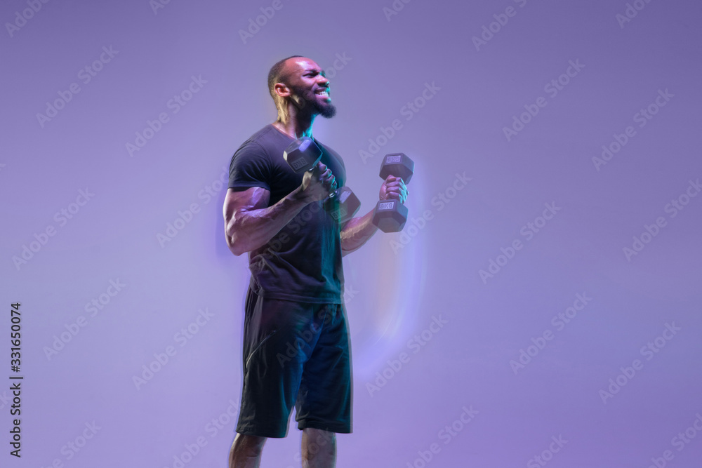 Emotions. Young african-american bodybuilder training over purple ...