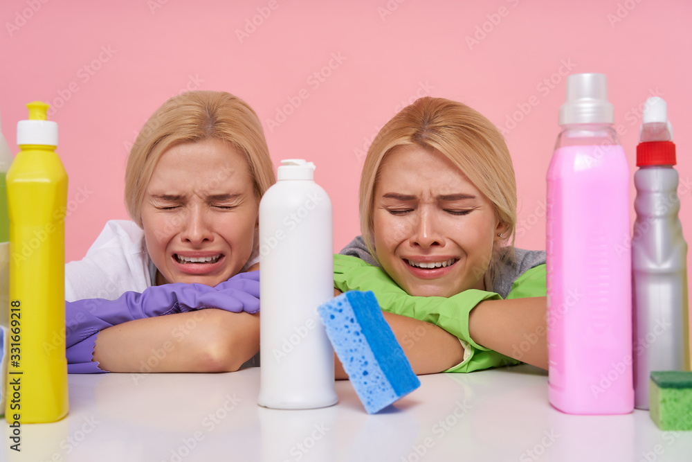 Unhappy young blonde cleaning ladies keeping their eyes closed while ...