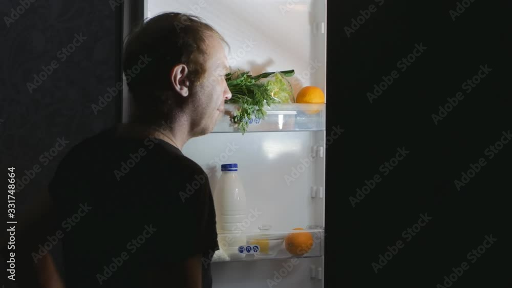 Video Stock a hungry young man opens the refrigerator at night and eats ...