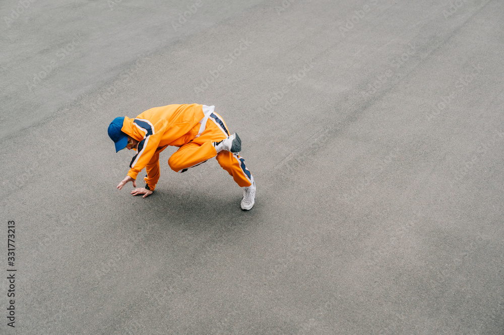 A bright dancer in an orange tracksuit shows a dance break performance ...