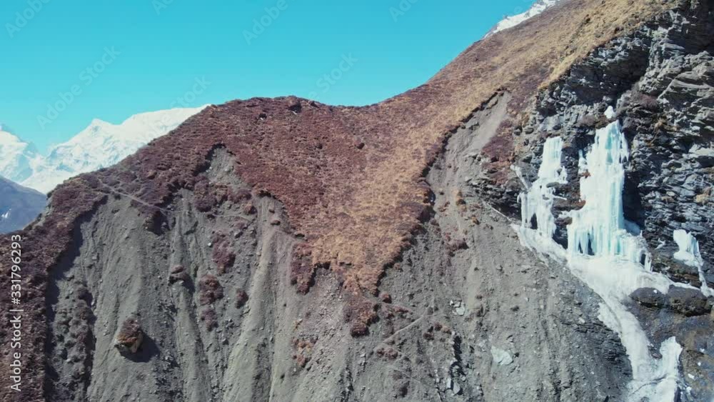 Waterfall falling from iced cliff, snow peak at horizon, river gorge ...
