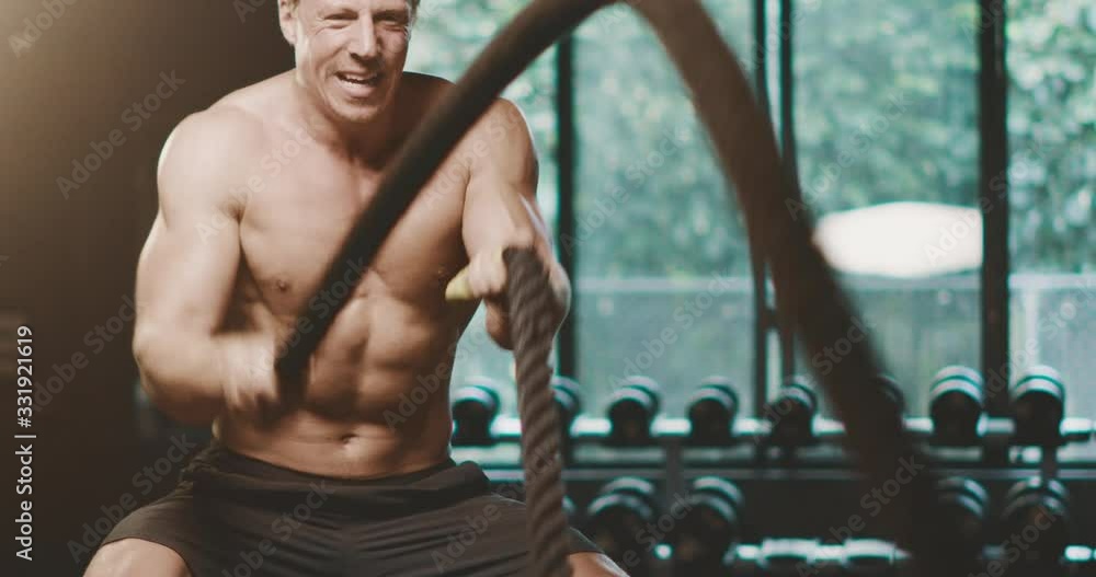 Attractive muscular man working out in the gym using battle ropes with ...