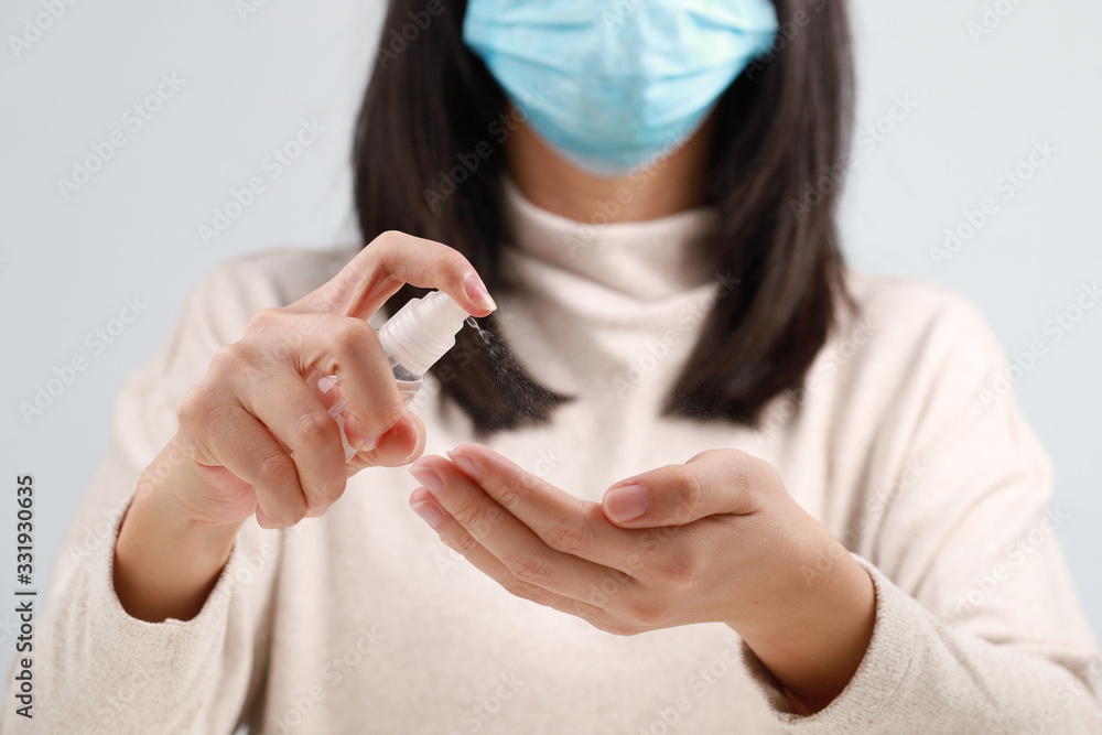 Female wearing protective face mask and applying alcohol spray or hand ...