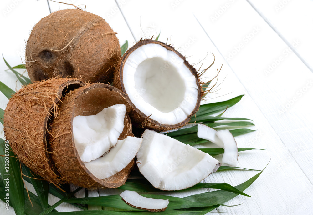 Coconut. Whole coconut, shell and green leaves on a white wooden ...