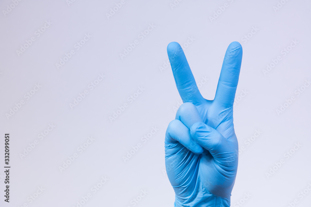 V sign is showed by right man hand in a blue medical glove on a white ...