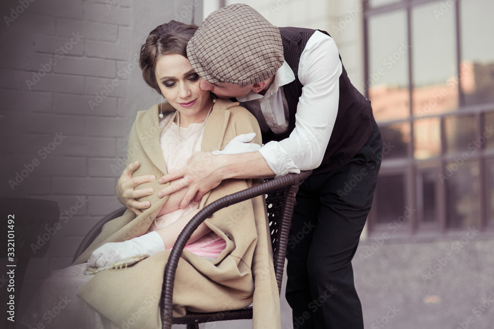 A young Man embraces a woman who is sitting on a wicker chair. Clothing ...