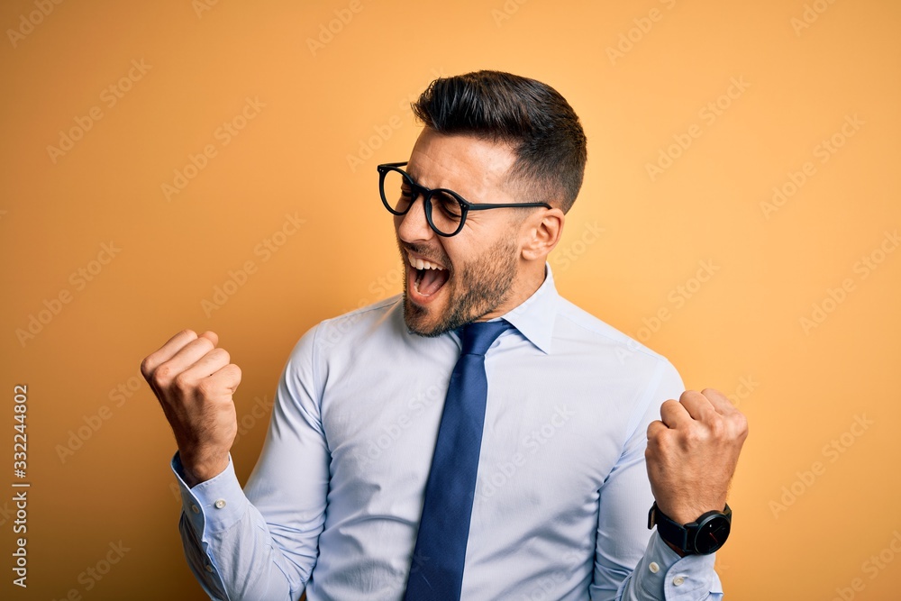 Young handsome businessman wearing tie and glasses standing over yellow ...