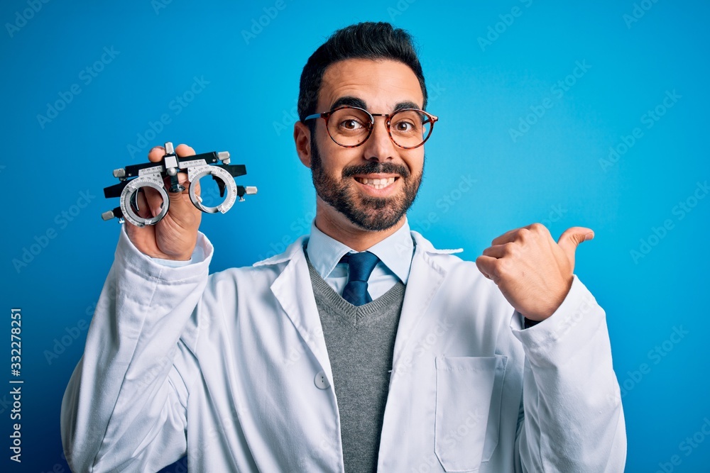Young handsome optical man with beard holding optometry glasses over ...