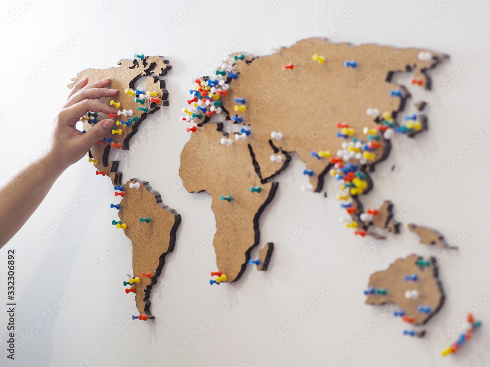 Woman hand putting red pin and marking location at wooden world map ...