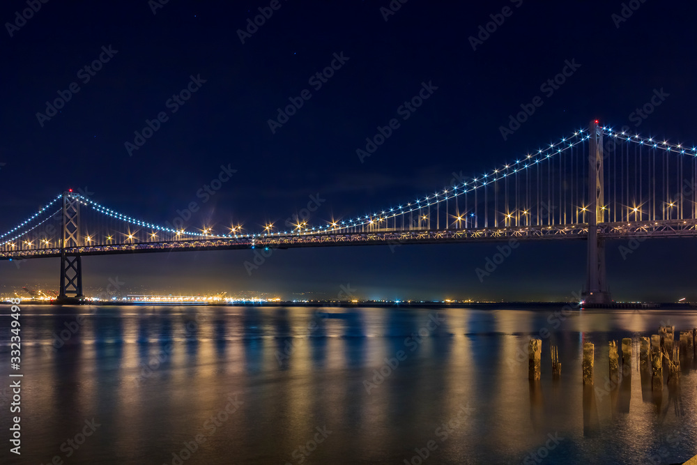 San Francisco Bay Bridge at night, lit up by yellow and blue lights ...