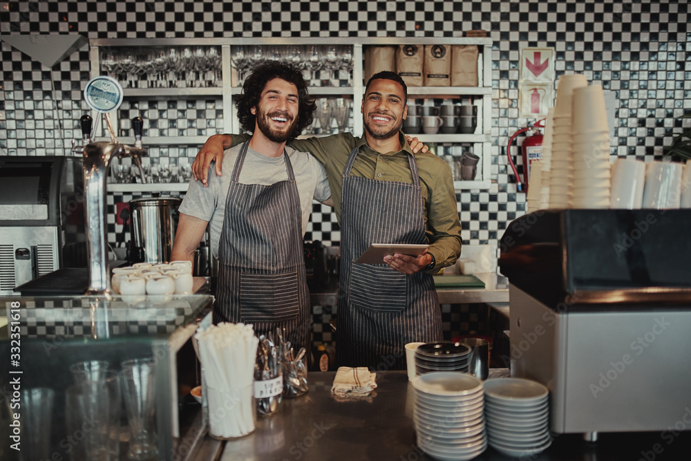 Portrait of smiling colleagues standing behind counter in cafe holding ...