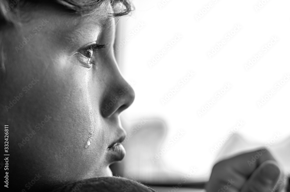 Profile of a sad crying boy with a tear on his cheek. The child is ...