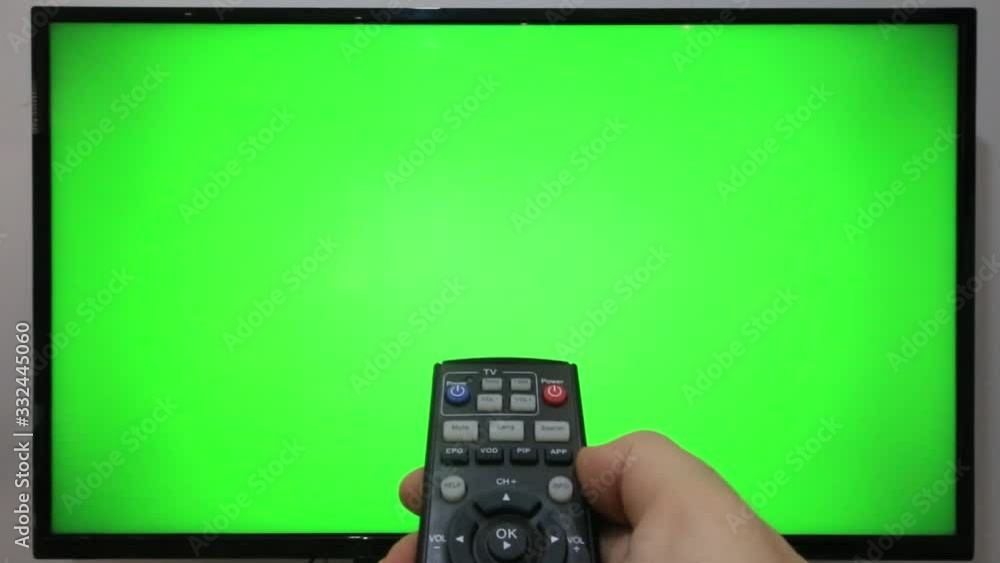 Person pointing a TV remote and pressing buttons in front of a TV with ...
