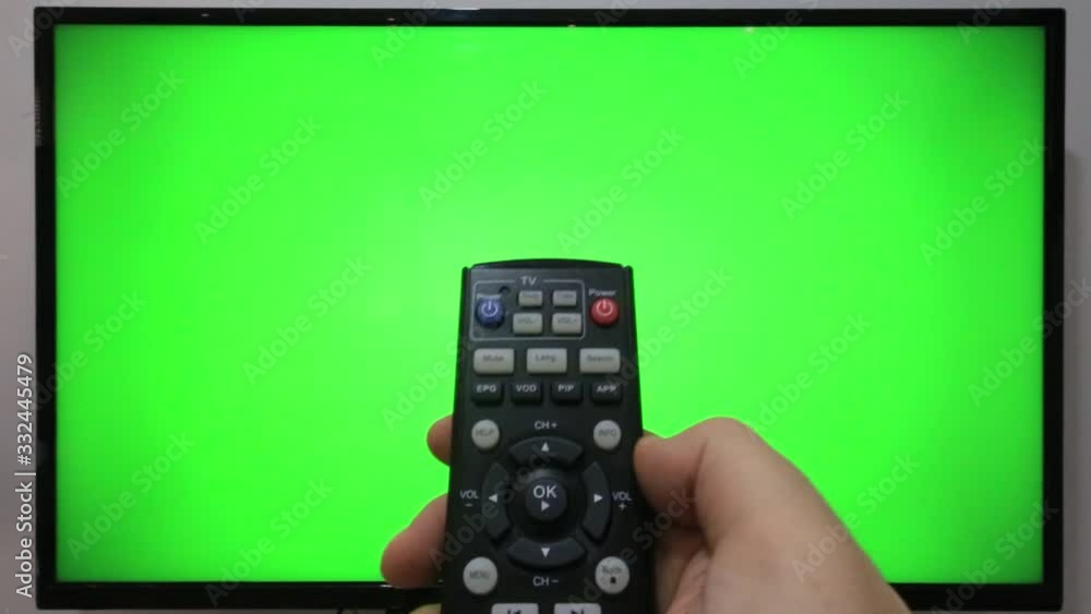 Person pointing a TV remote and pressing buttons in front of a TV with ...
