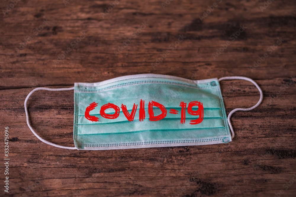 Medical face mask that reads covid-19 on wooden plank surface. General personal protective ...