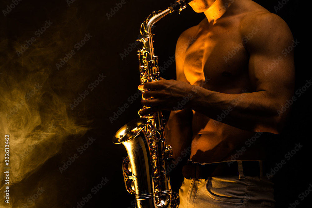 Muscular man with naked torso playing on saxophone with smoked colorful ...