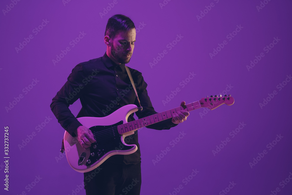 Young and joyful caucasian musician playing guitar on gradient purple ...