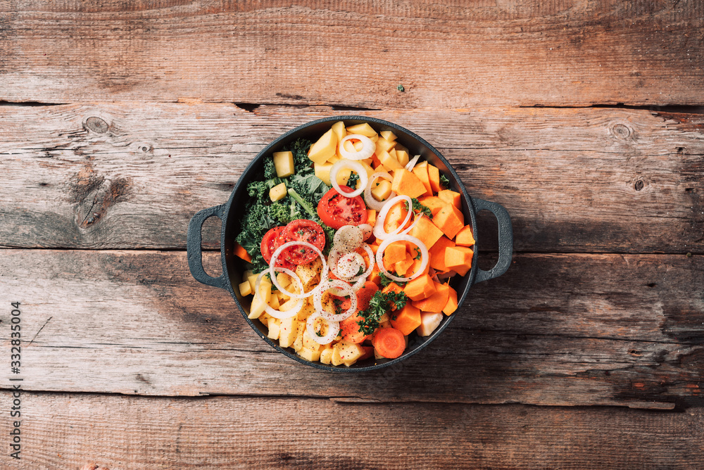 Big pot with sliced colorful vegetables and cooking utensils on rustic ...