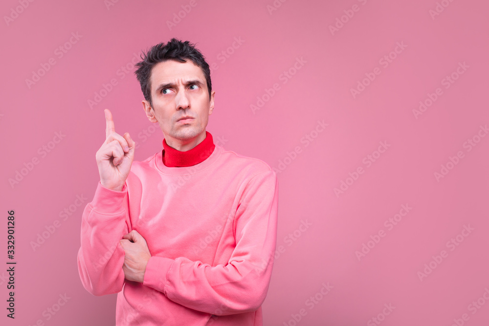 Serius concentrated young man in pink sweater point up with smart face ...