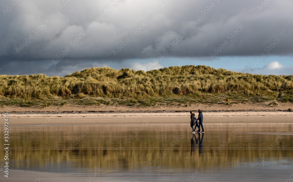 Family walking by grassy sand dunes on Banna beach on the west coast of ...