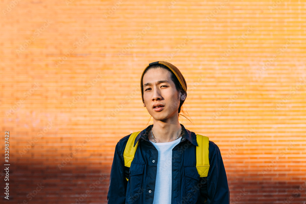 Portrait of stylish young chinese man posing in front of a brick wall ...