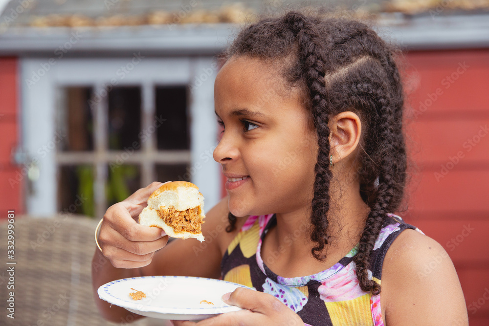 Pretty child holding and eating a pulled pork sandwich as she stands ...
