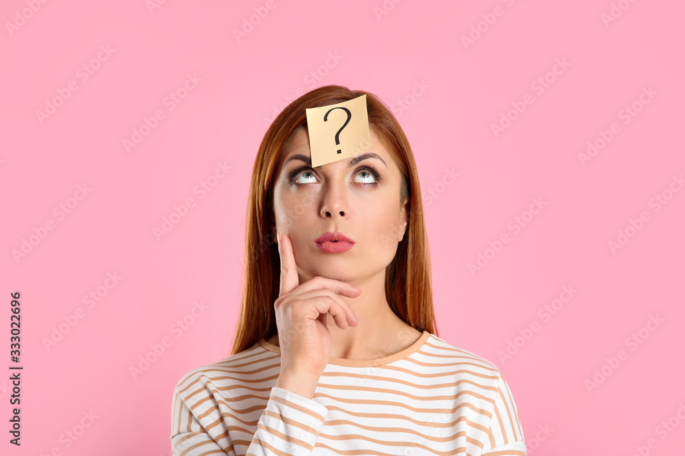 Emotional woman with question mark sticker on forehead against pink ...