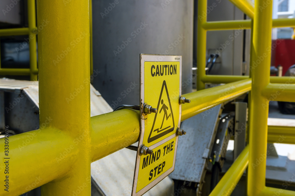 Signage with icon and letter 'Caution Mind The Step' on a handrail on ...