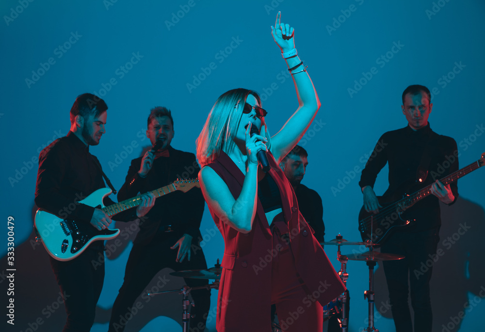 Young caucasian musicians, band performing on blue studio background in ...