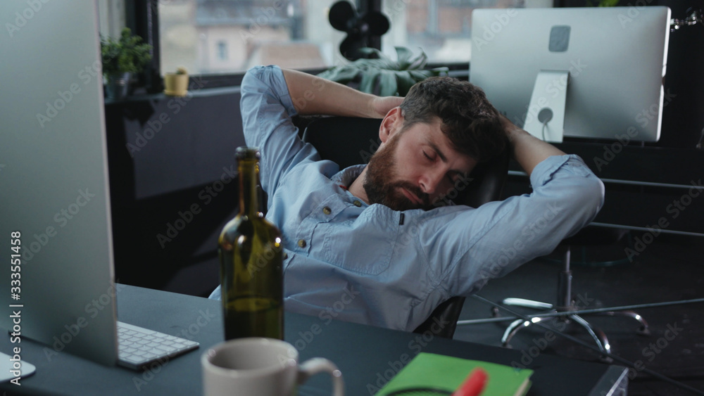 Drunk exhausted young man falling asleep in chair at office table ...