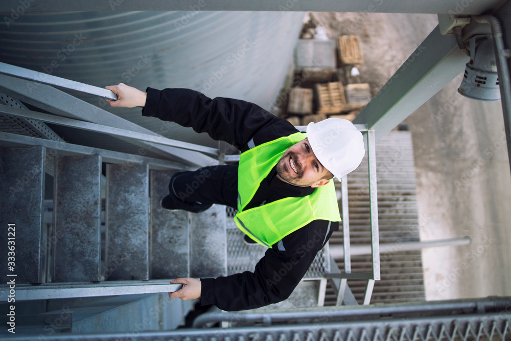 Top view of factory worker climbing metal stairs on industrial silo ...