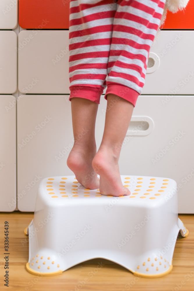 Small kids legs and feet tippy-toes on a step stool to reach for ...