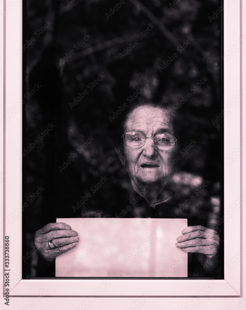 Old sad woman showing empty signboard at the window in silent request ...