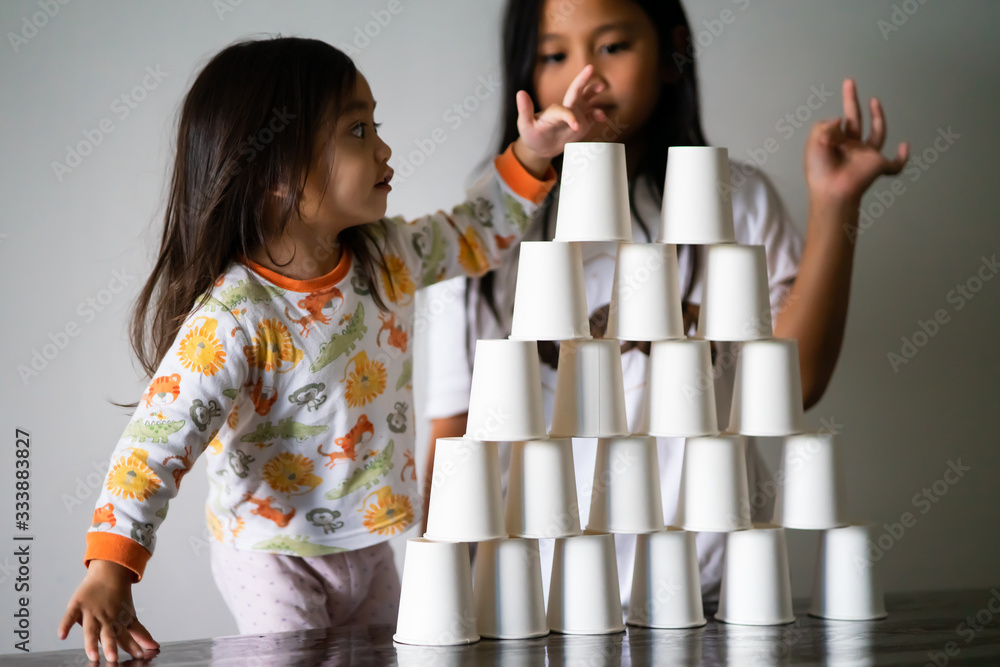 Kids Playing with white paper cups building a cup tower on the table ...