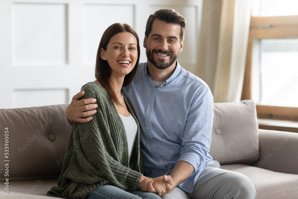 Portrait Of Happy Young Married Couple Sitting On Sofa Embracing