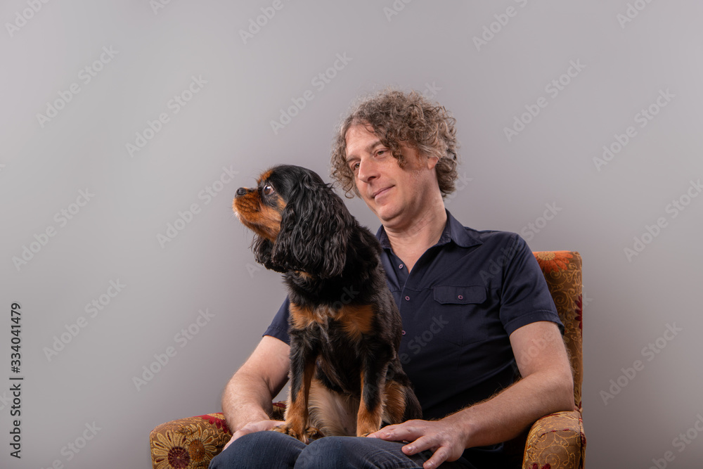 A cute dog in focus, sitting on its owner's lap. The dog looks to its ...