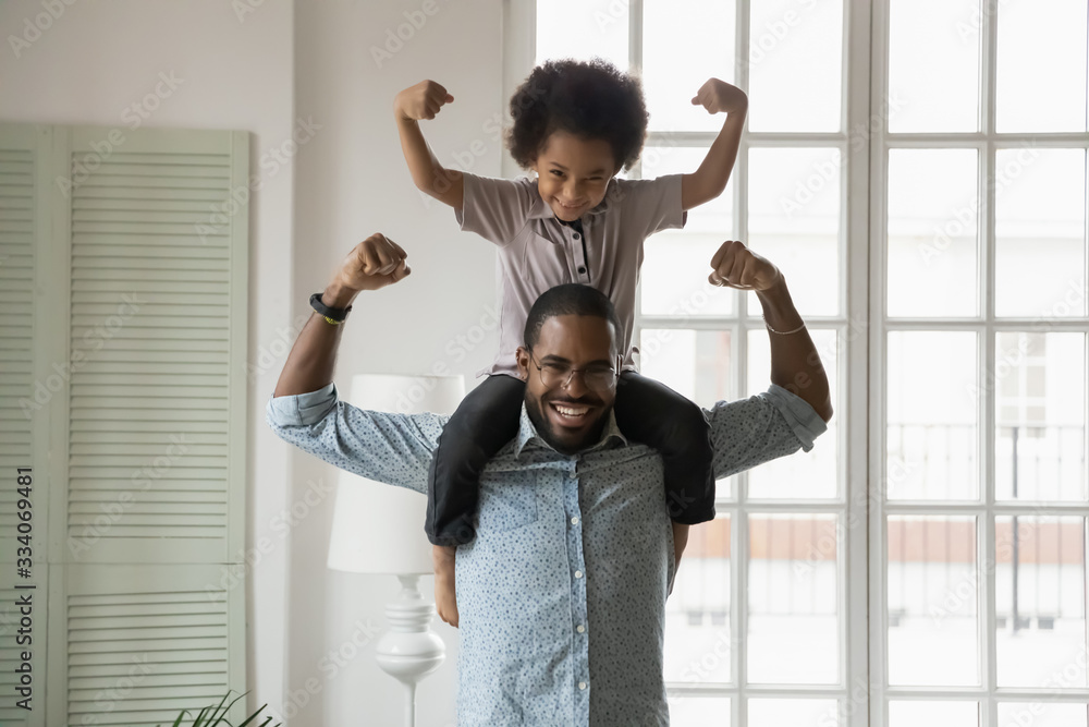 Foto de Small son sit on strong dad shoulders showing biceps. African ...