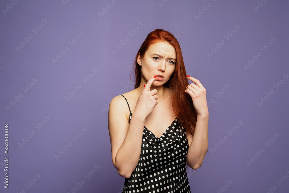 An embarrassed and surprised pretty woman stands on a lilac background ...