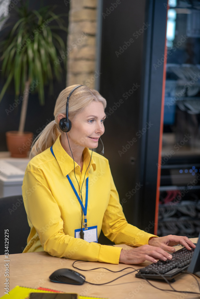 Blonde woman sitting in front of computer in headphones, typing Stock ...