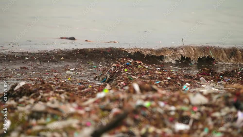 Slow motion. Plastic trash and garbage dumped on dark sand of the beach ...