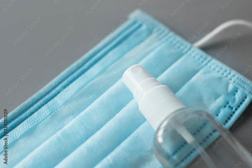 Bottle with alcohol gel antiseptic and medical face mask on a grey ...