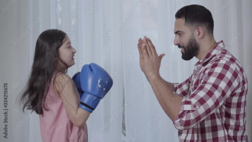 Side view of confident little Middle Eastern girl boxing father's hands ...