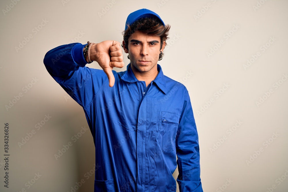 Young mechanic man wearing blue cap and uniform standing over isolated ...