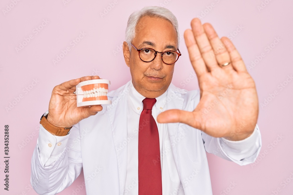 Middle age senior grey-haired dentist man holding prosthesis denture ...